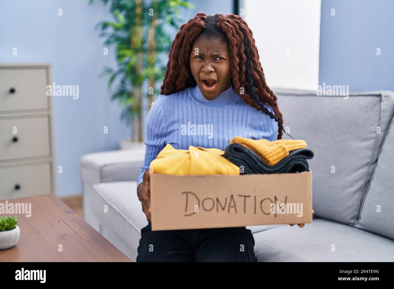 African woman holding donations box for charity angry and mad screaming ...