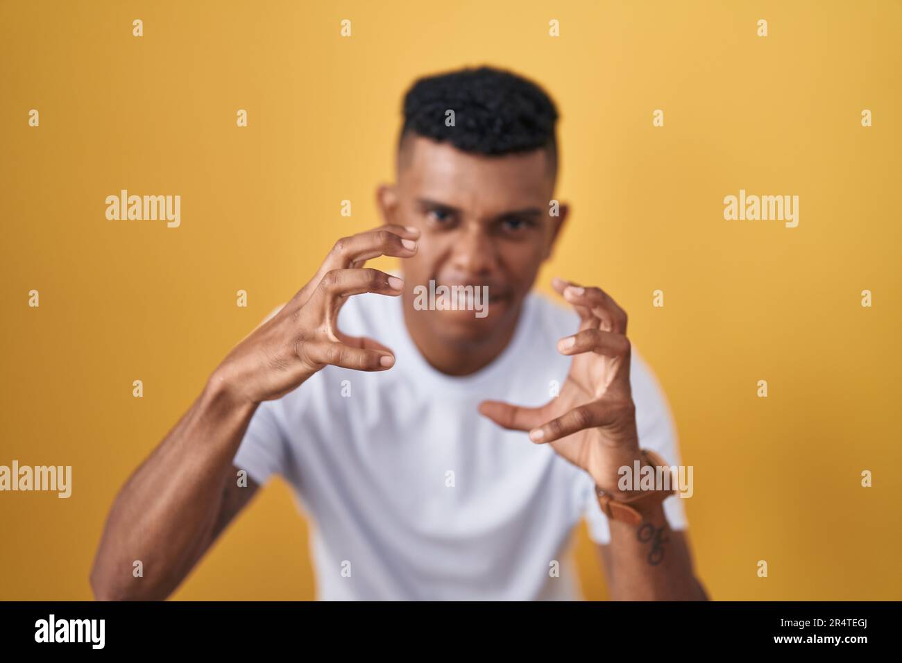 Young hispanic man standing over yellow background shouting frustrated ...