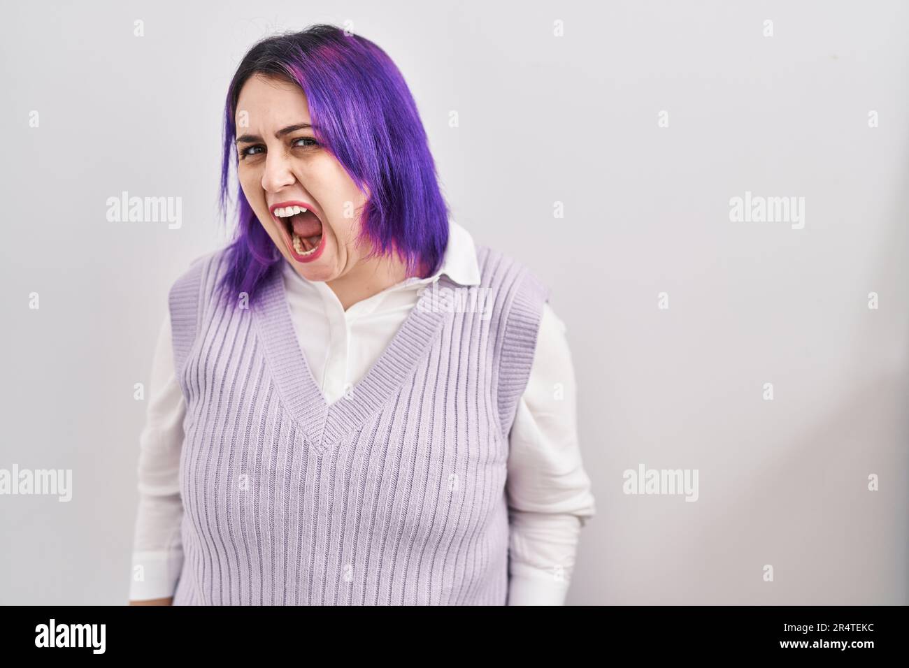 Plus size woman wit purple hair standing over white background angry ...