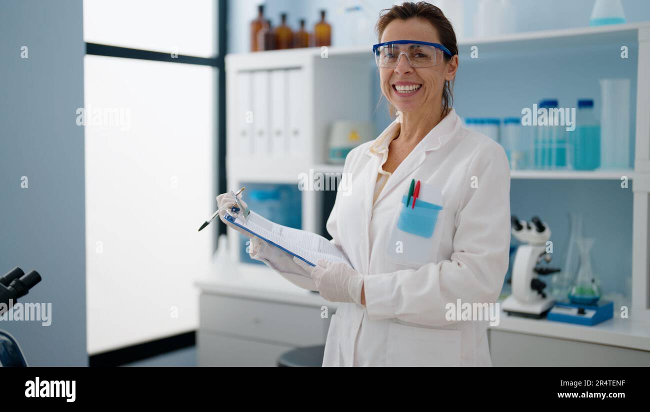 Middle age hispanic woman wearing scientist uniform holding checklist ...