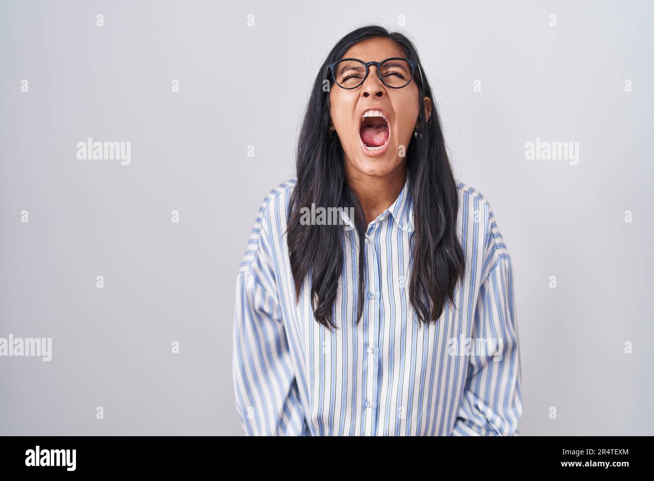 Young hispanic woman wearing glasses angry and mad screaming frustrated ...
