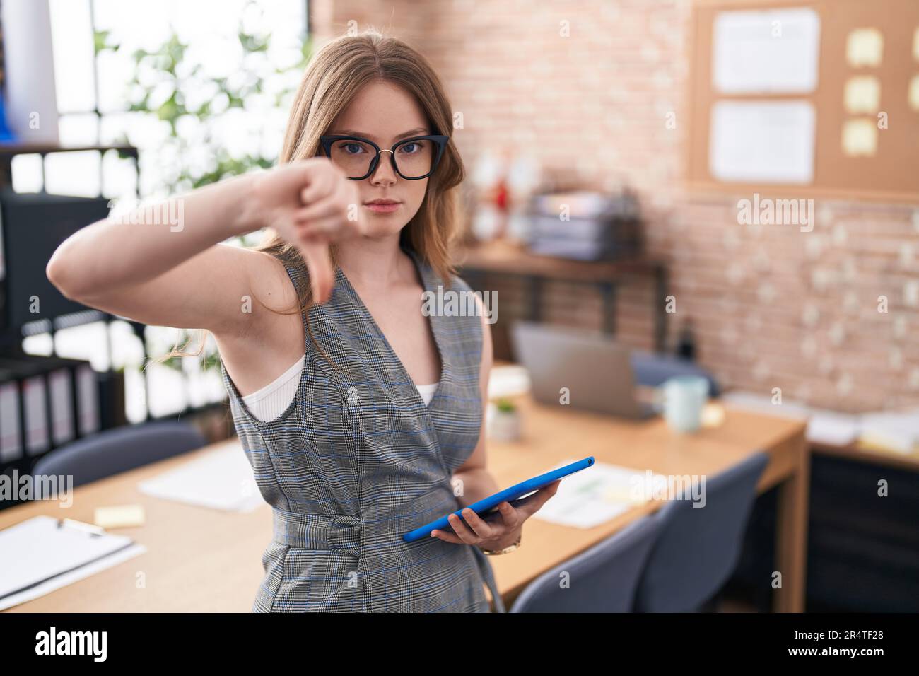 Caucasian woman working at the office wearing glasses looking unhappy ...
