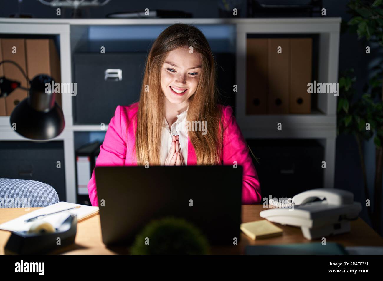 Young caucasian woman working at the office at night praying with hands ...
