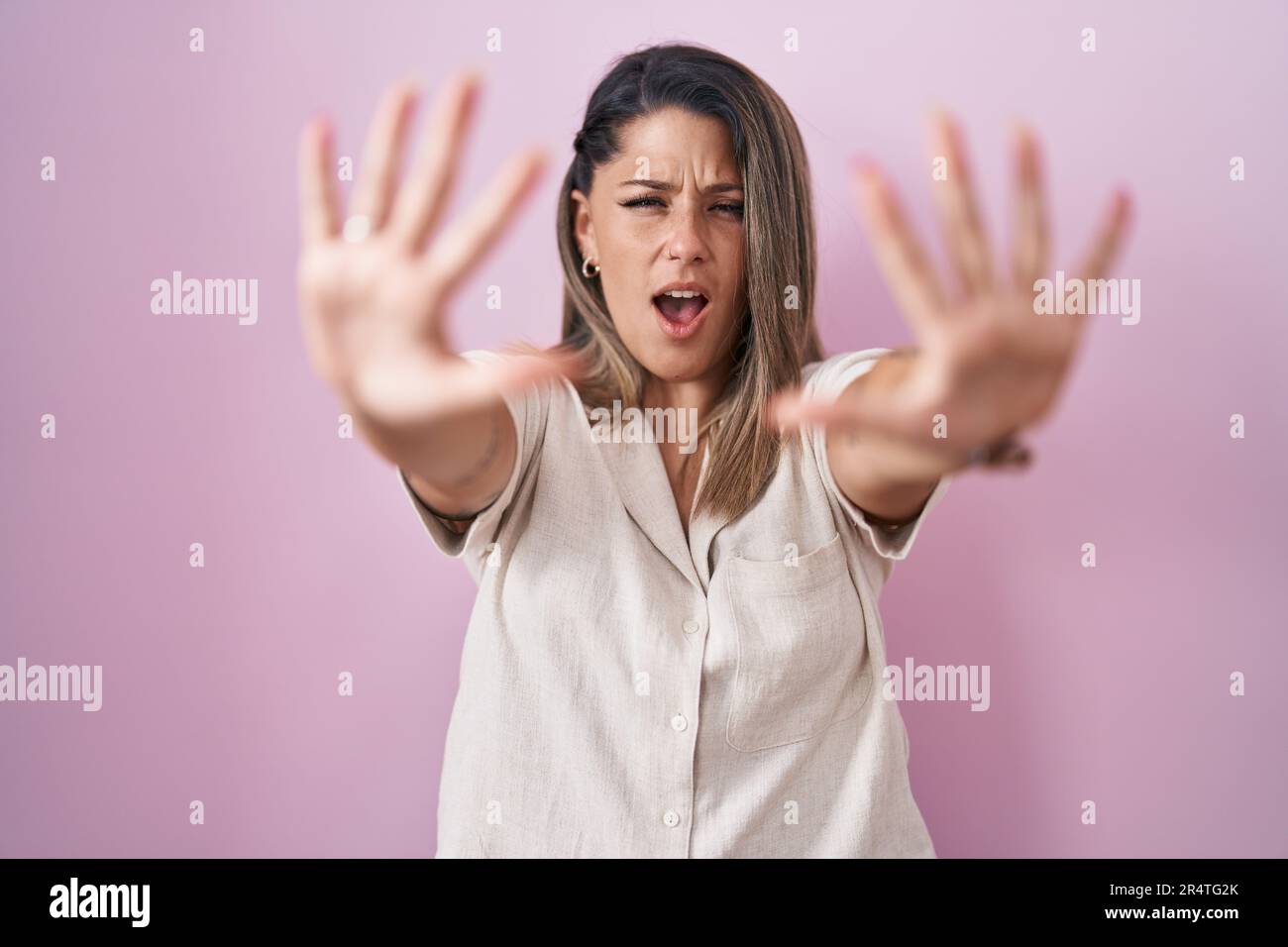 Blonde woman standing over pink background doing stop gesture with ...
