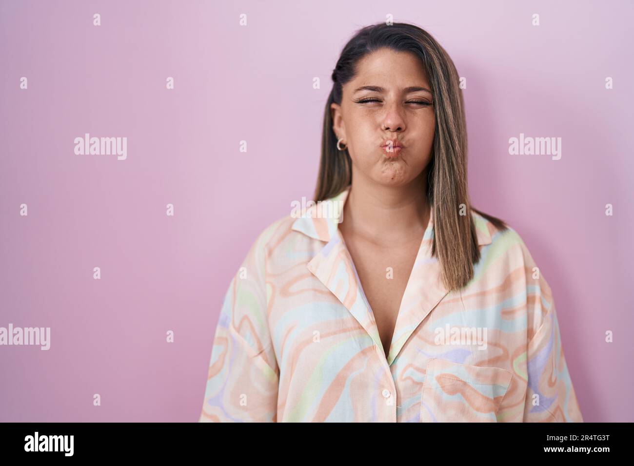 Blonde woman standing over pink background puffing cheeks with funny ...