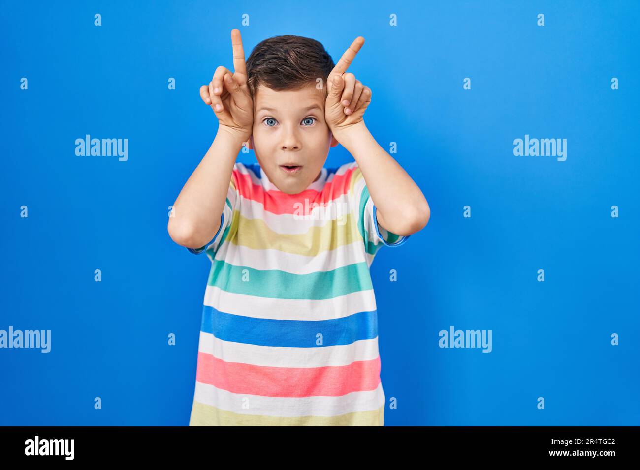 Young caucasian kid standing over blue background doing funny gesture ...