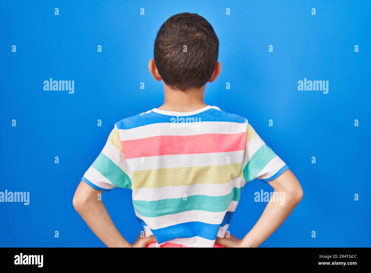 Young caucasian kid standing over blue background standing backwards ...