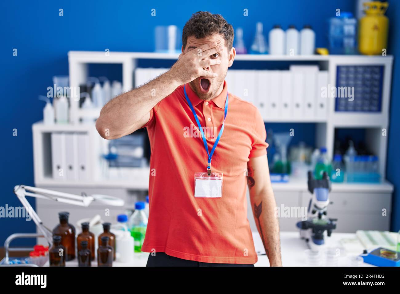 Young hispanic man working at scientist laboratory peeking in shock ...