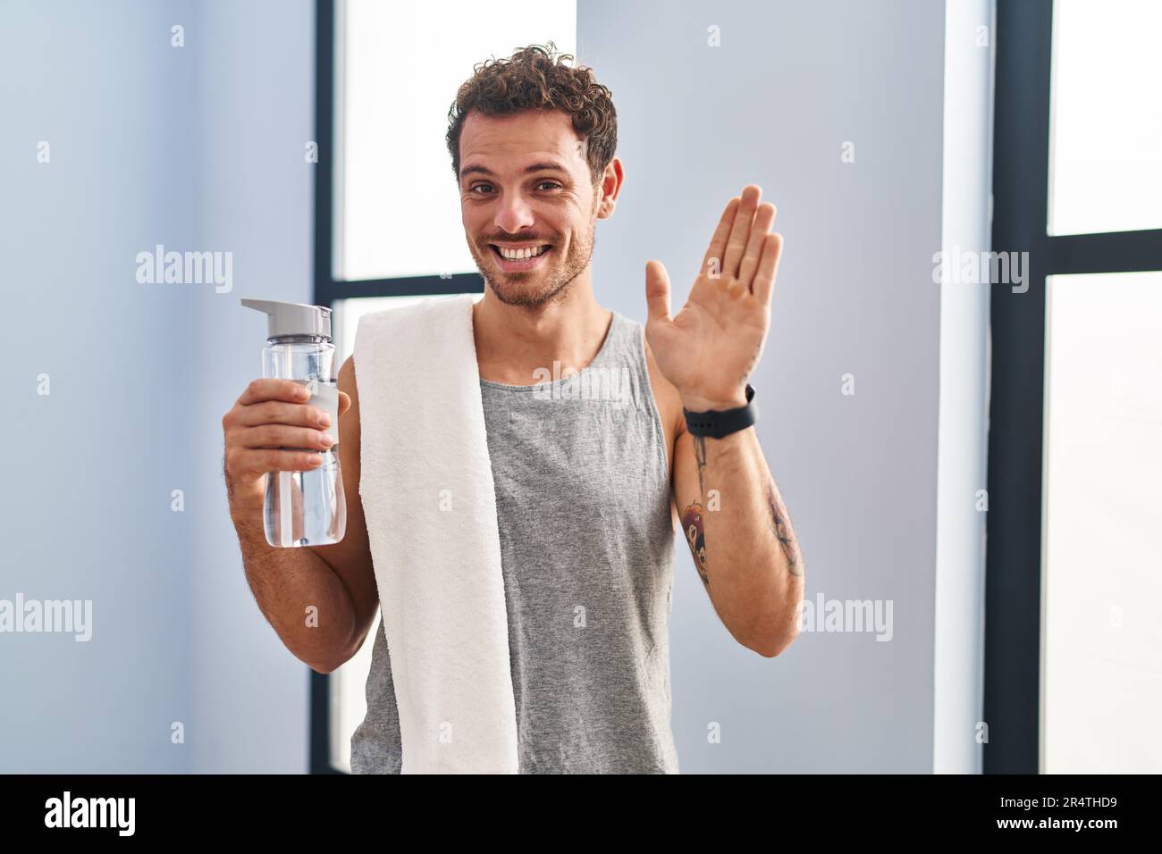 Young hispanic man wearing sportswear drinking water waiving saying ...