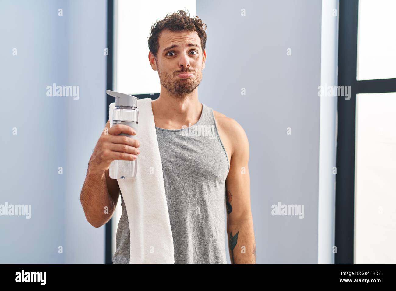 Young hispanic man wearing sportswear drinking water depressed and ...