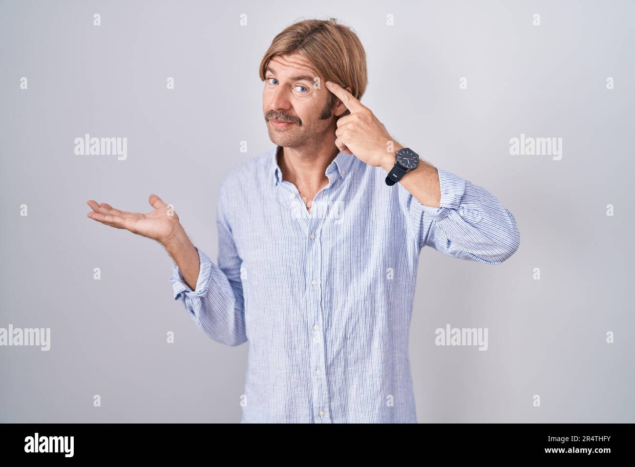 Caucasian man with mustache standing over white background confused and ...