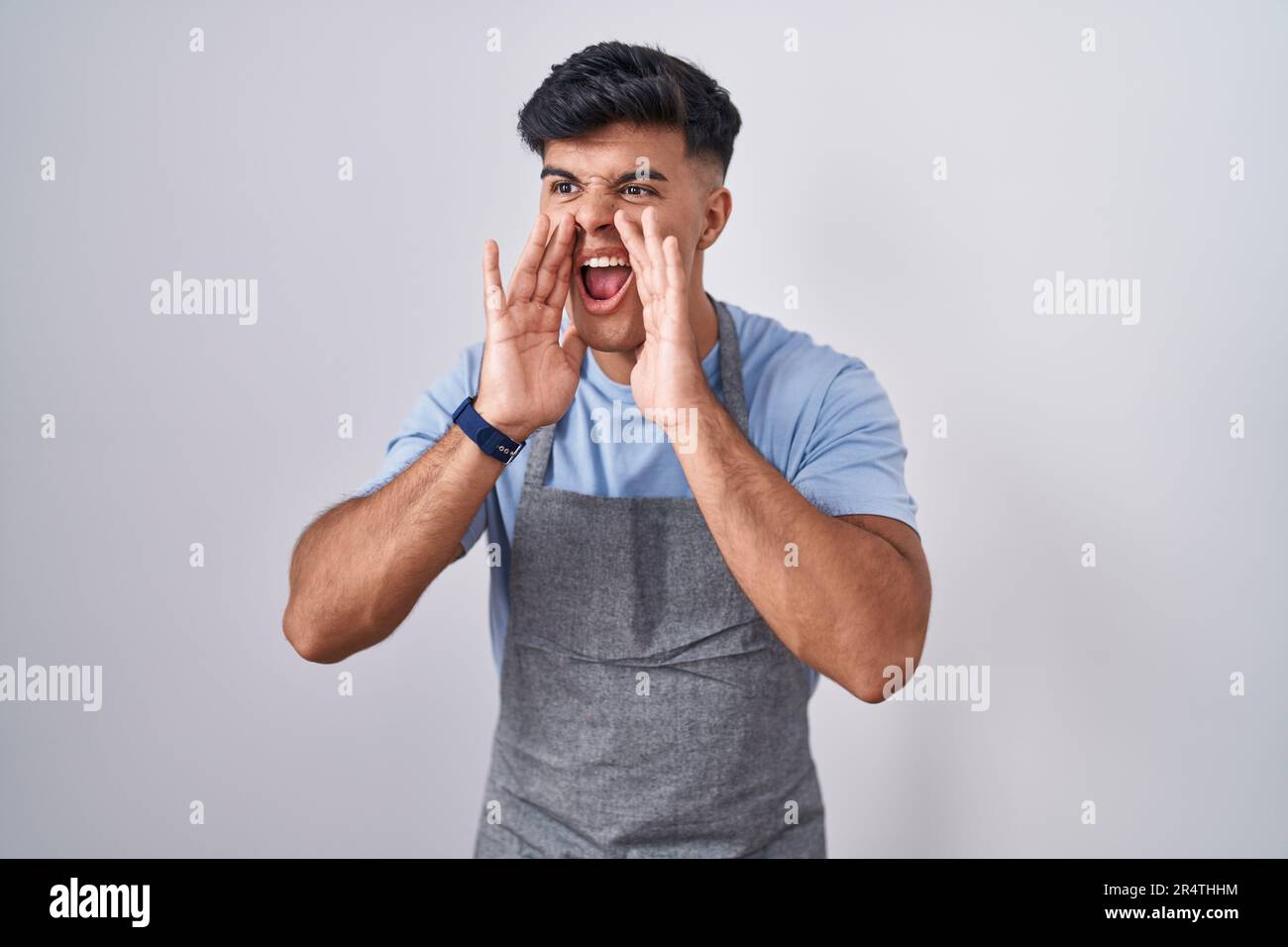 Hispanic young man wearing apron over white background shouting angry ...