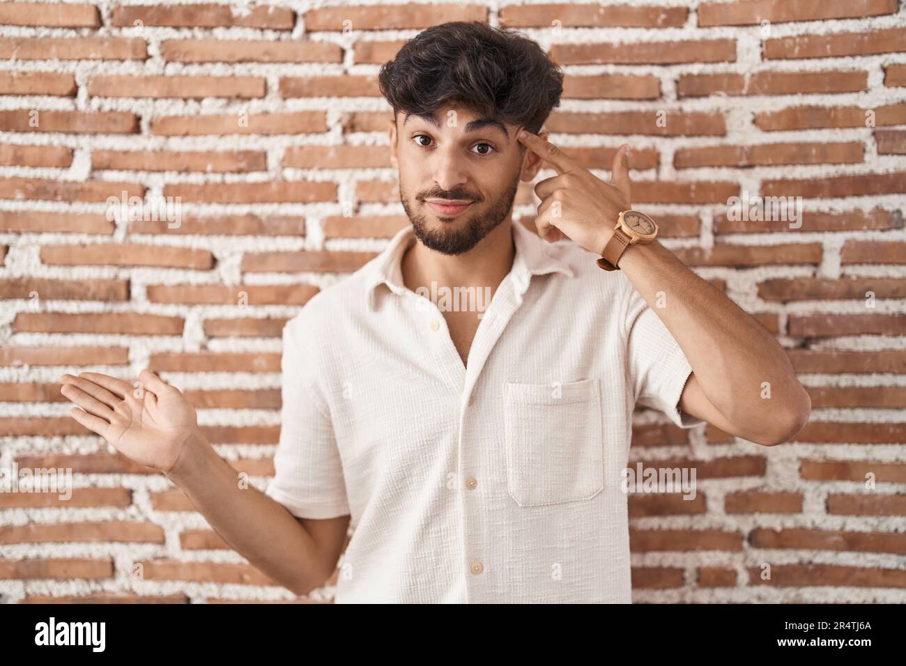 Arab man with beard standing over bricks wall background confused and ...