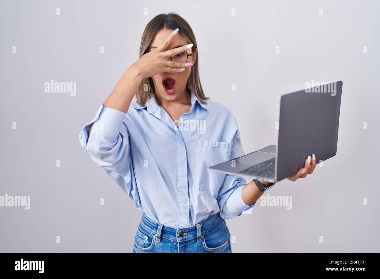 Young woman working using computer laptop peeking in shock covering ...