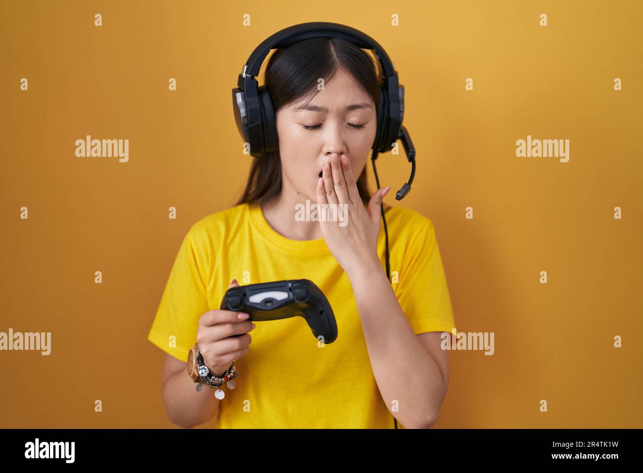 Chinese young woman playing video game holding controller bored yawning ...