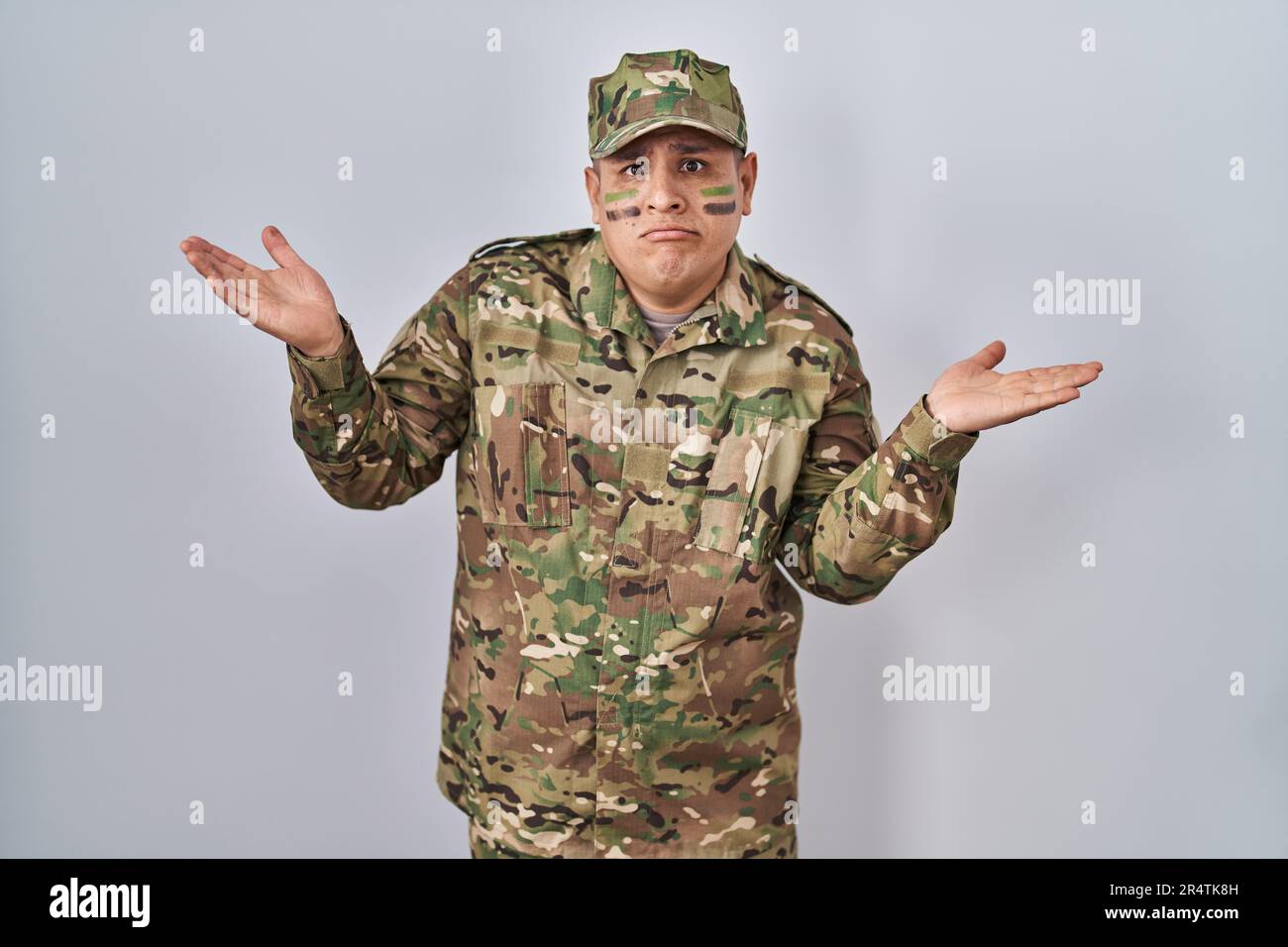 Hispanic young man wearing camouflage army uniform clueless and ...