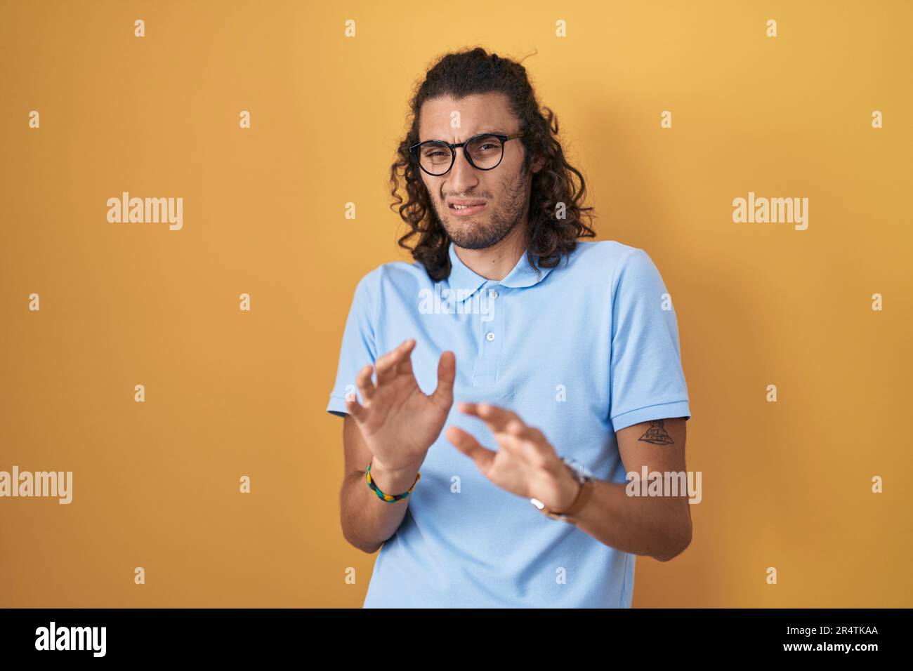 Young hispanic man standing over yellow background disgusted expression ...