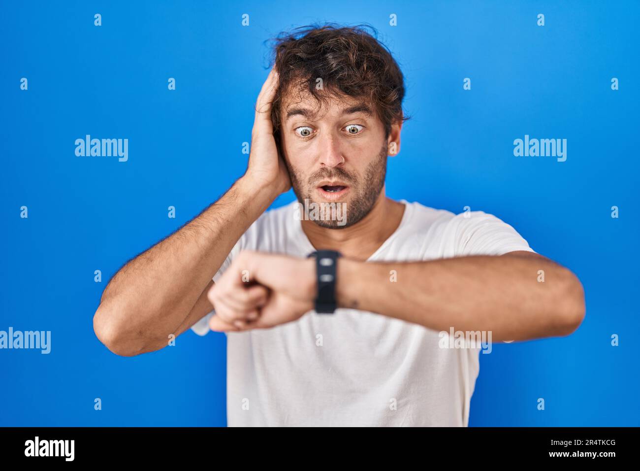 Hispanic young man standing over blue background looking at the watch ...