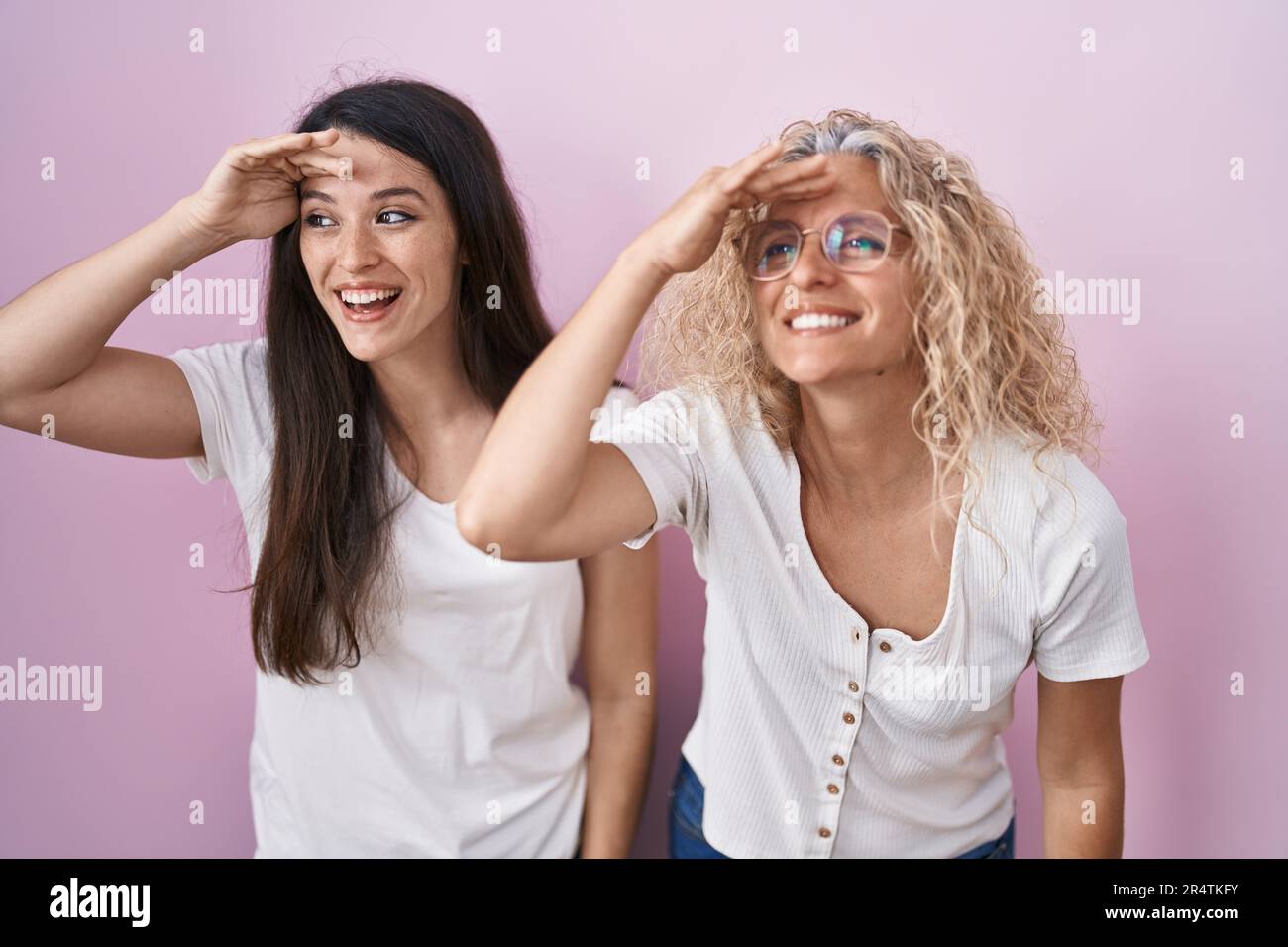 Mother and daughter standing together over pink background very happy ...