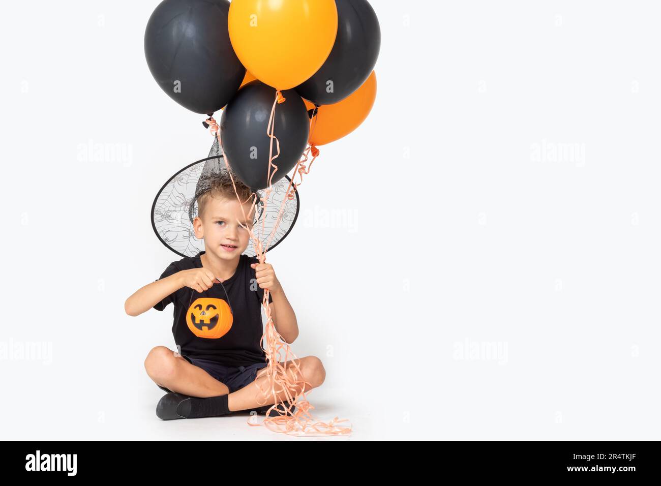 A cheerful happy boy in a wizard's hat holding a pumpkin-shaped bucket ...