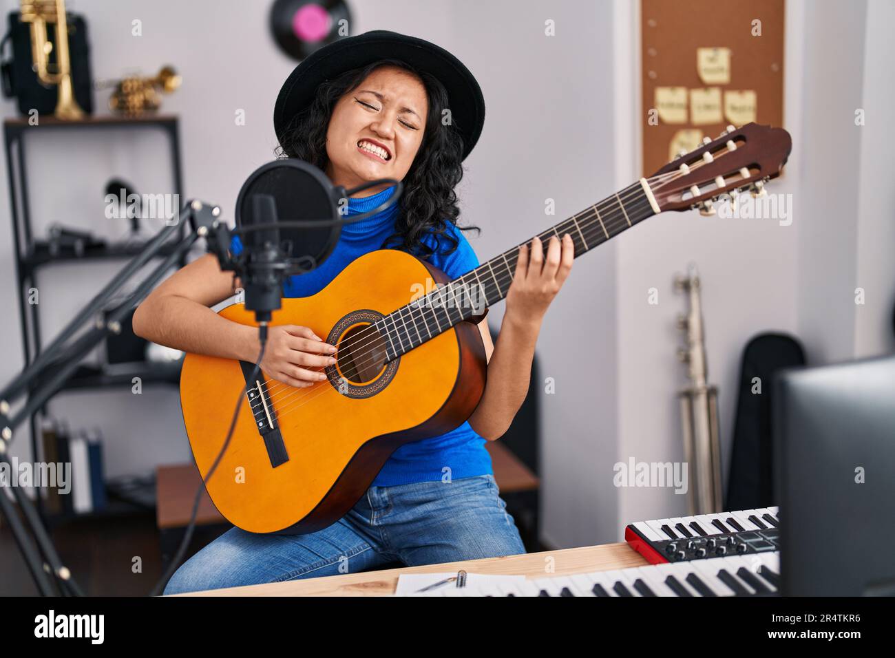 Young chinese woman artist singing song playing guitar at music studio ...