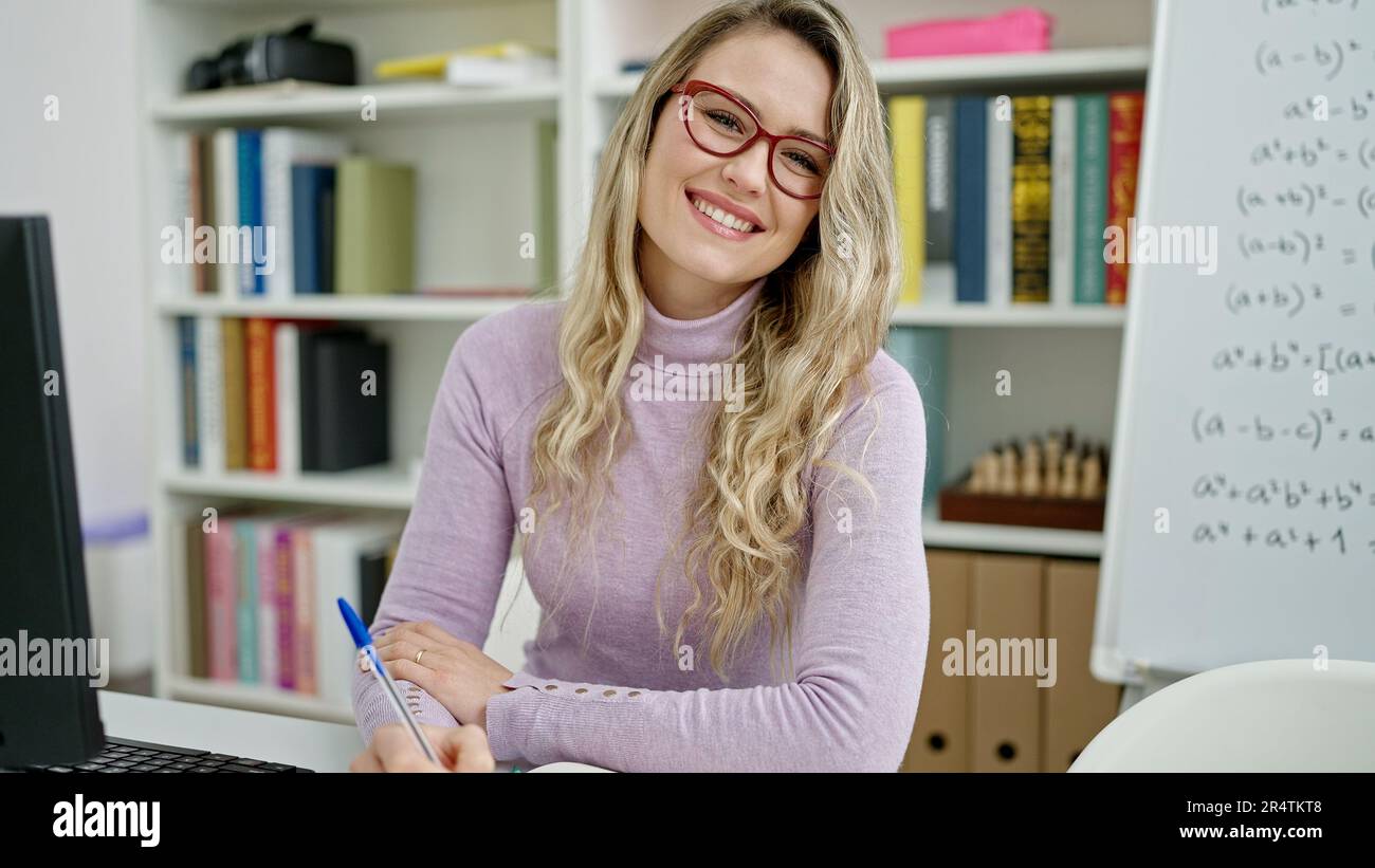 Young blonde woman student using computer writing on notes at classroom ...