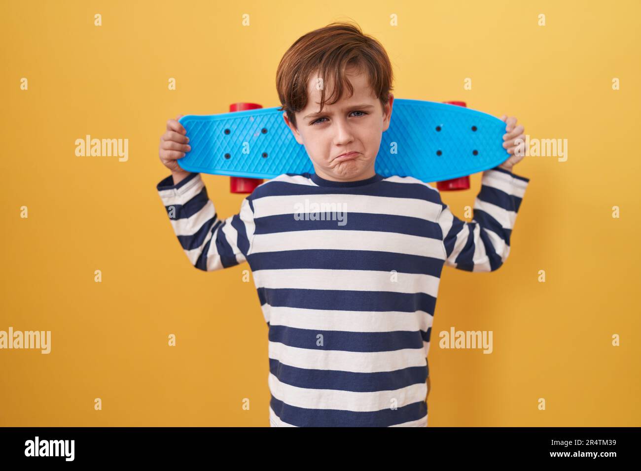 Little caucasian boy holding skate over yellow background depressed and ...