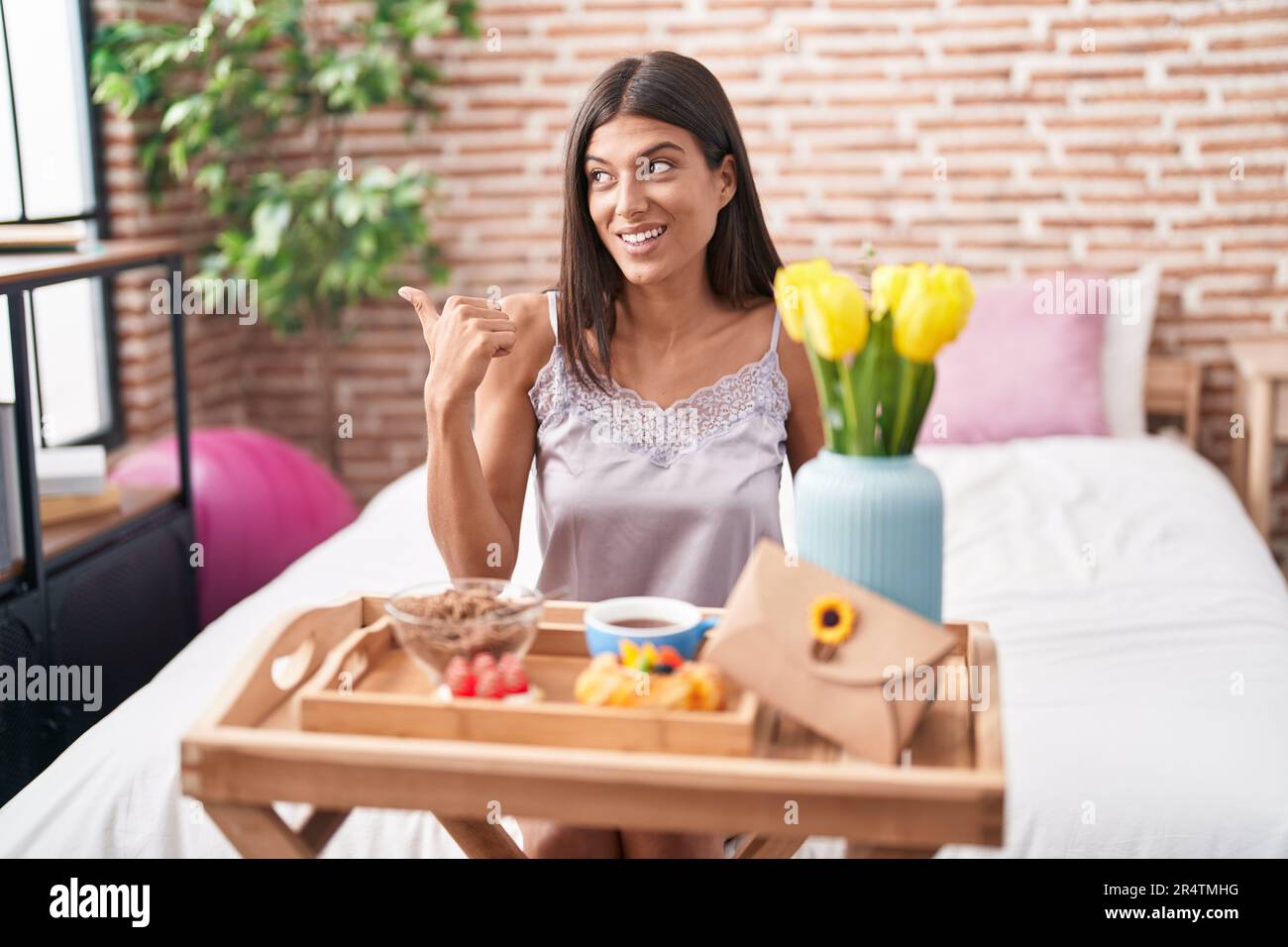 Brunette young woman eating breakfast sitting on the bed smiling with ...
