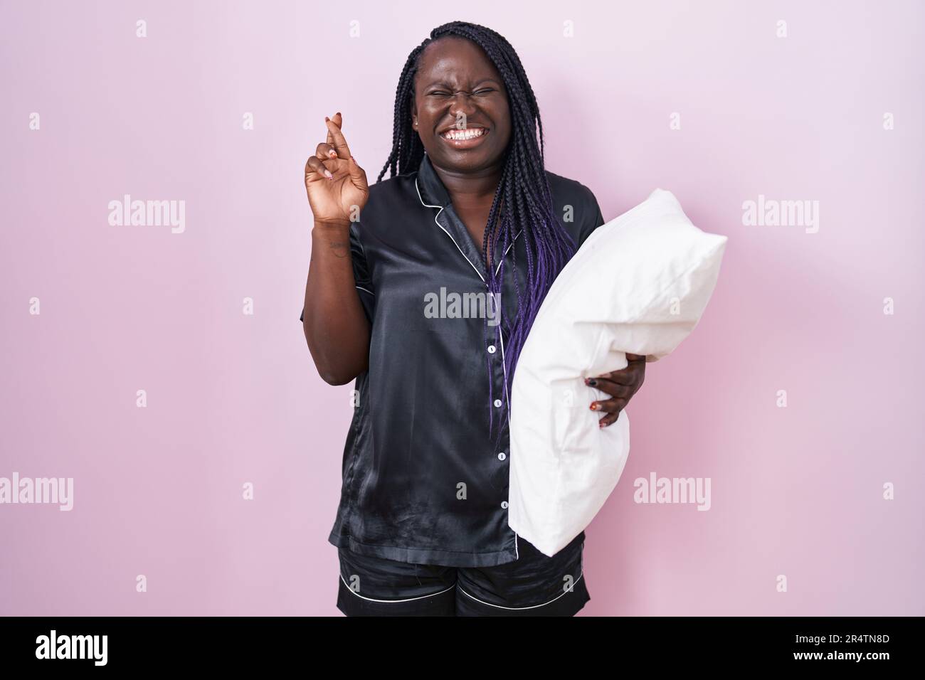 Young african woman wearing pijama hugging pillow gesturing finger ...