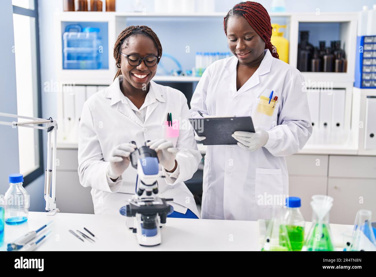African american women scientists using microscope writing on document at laboratory Stock Photo ...