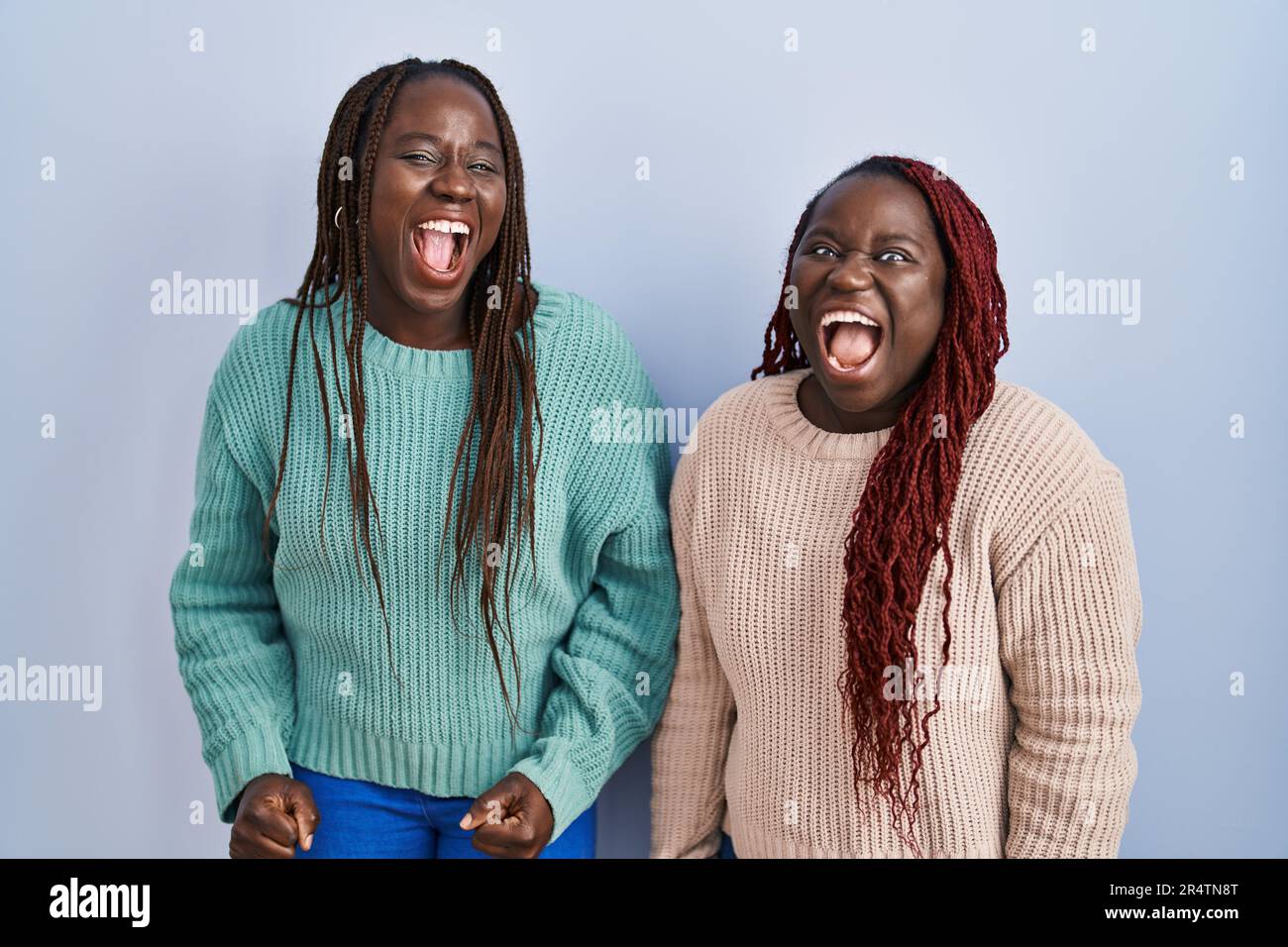 Two african woman standing over blue background angry and mad screaming ...