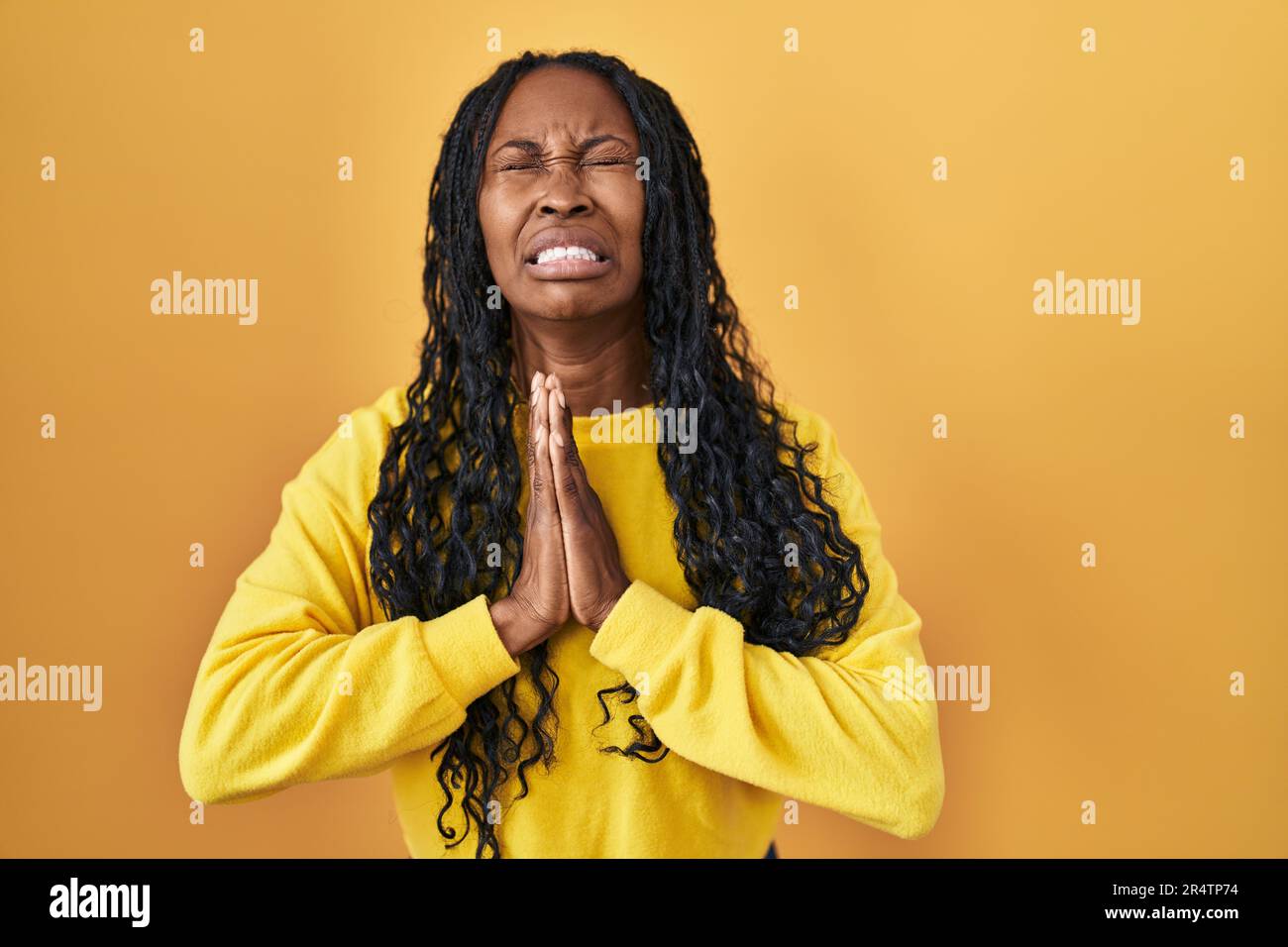 African woman standing over yellow background begging and praying with ...