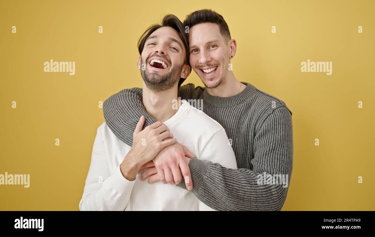 Two men couple hugging each other standing over isolated yellow ...