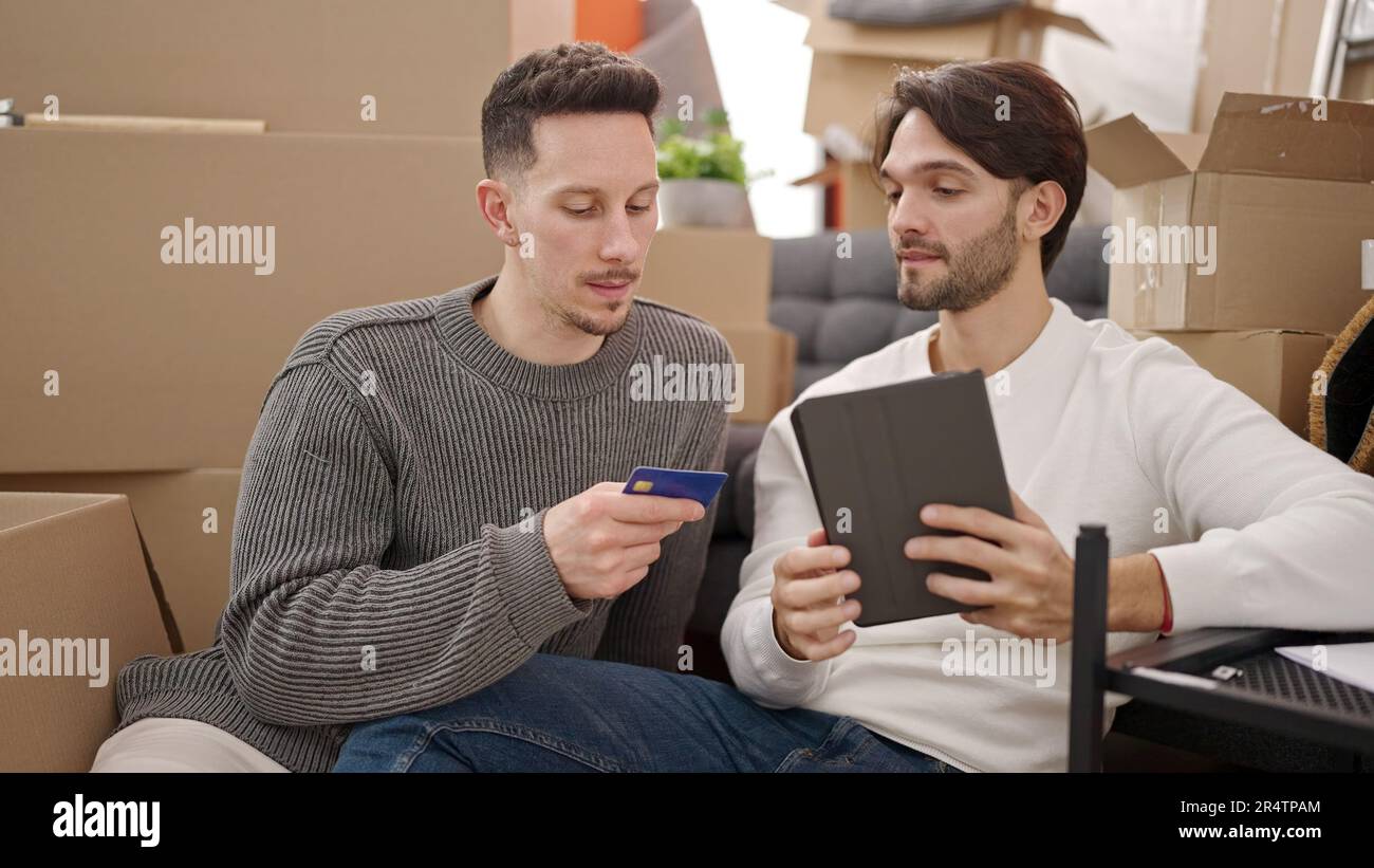 Two men couple shopping with touchpad and credit card sitting on floor ...