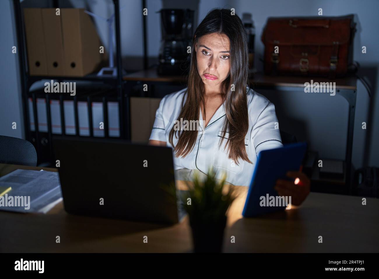 Young brunette woman working at the office at night depressed and worry ...