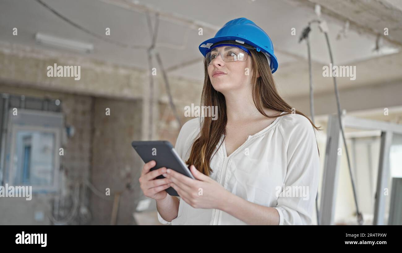 Young beautiful hispanic woman builder using touchpad at construction ...