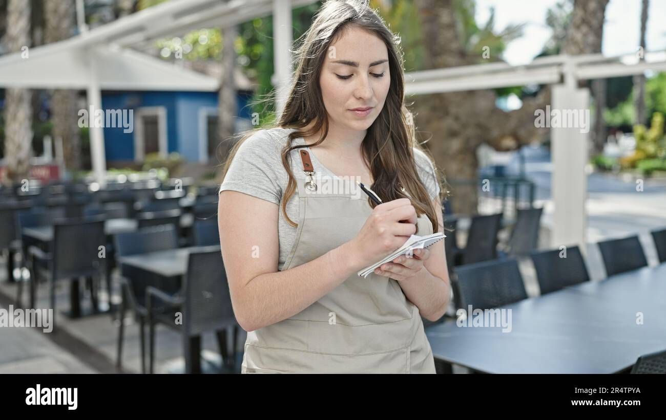 Young beautiful hispanic woman waitress taking notes at coffee shop ...
