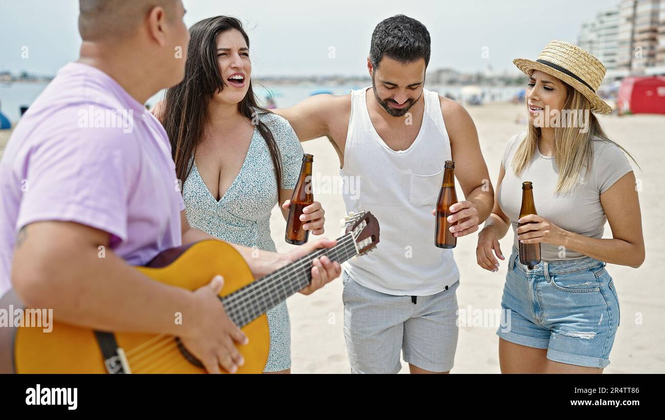 Group of people playing guitar drinking beer singing song at beach ...