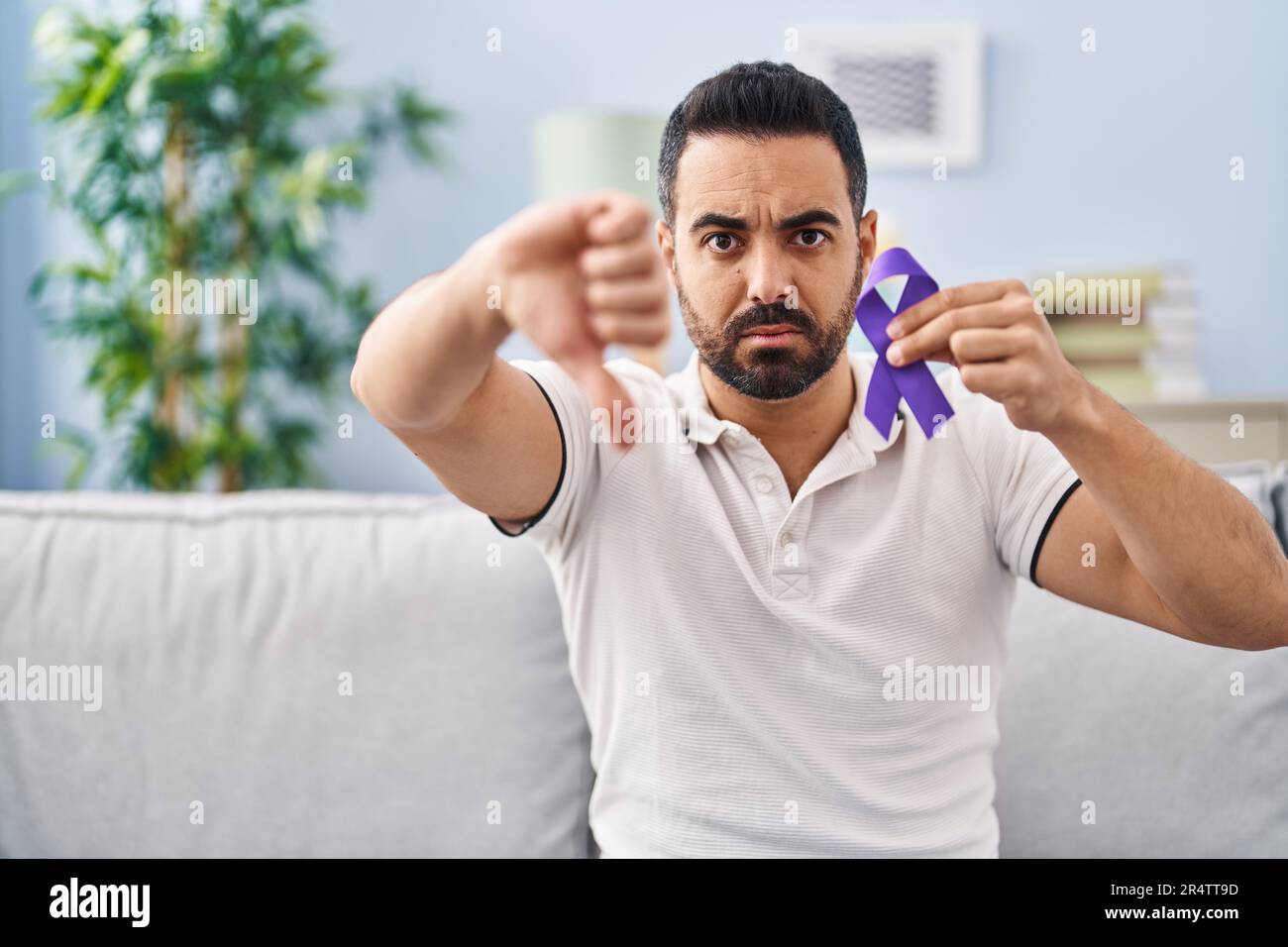 Young hispanic man with beard holding purple ribbon awareness with ...