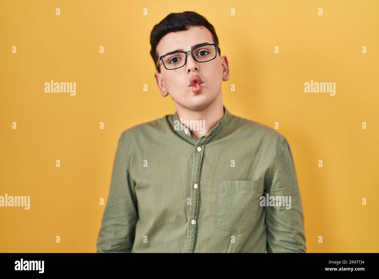 Non binary person standing over yellow background making fish face with ...
