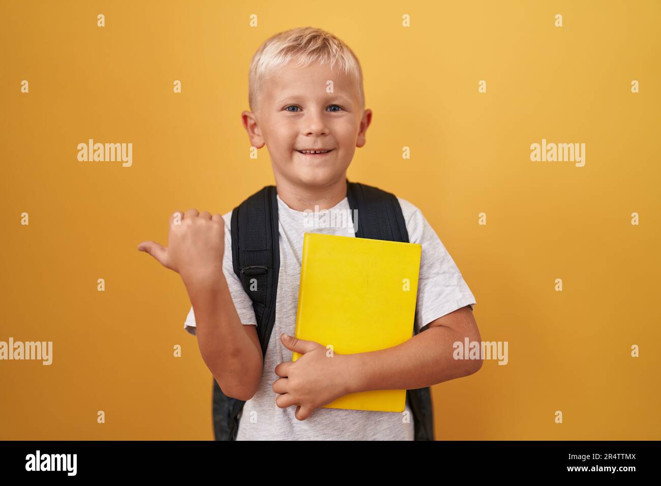 Little caucasian boy wearing student backpack and holding book pointing ...