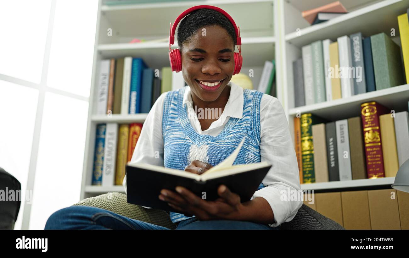 African american woman student listening to music reading book at ...
