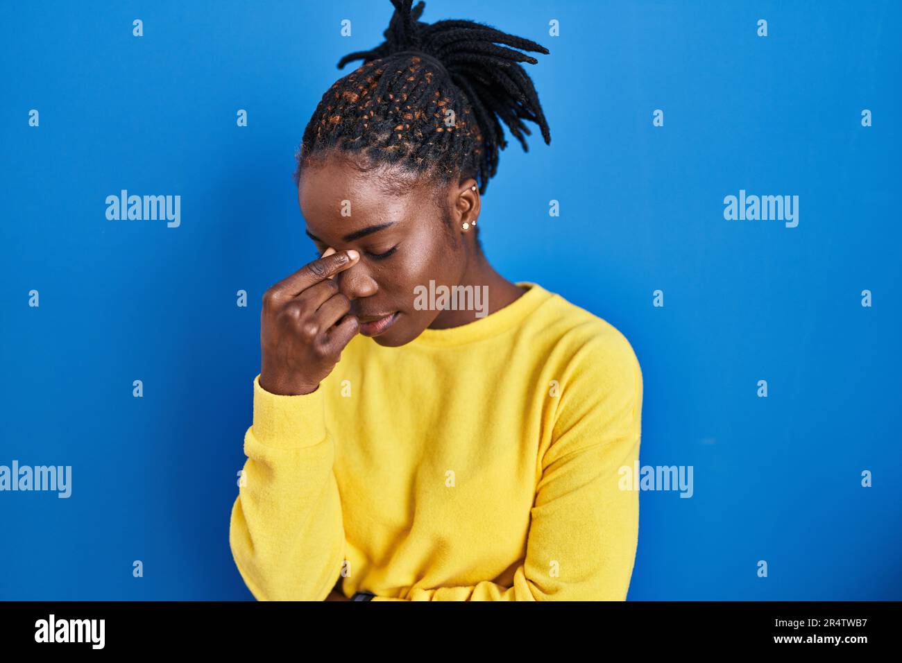 Beautiful black woman standing over blue background tired rubbing nose ...