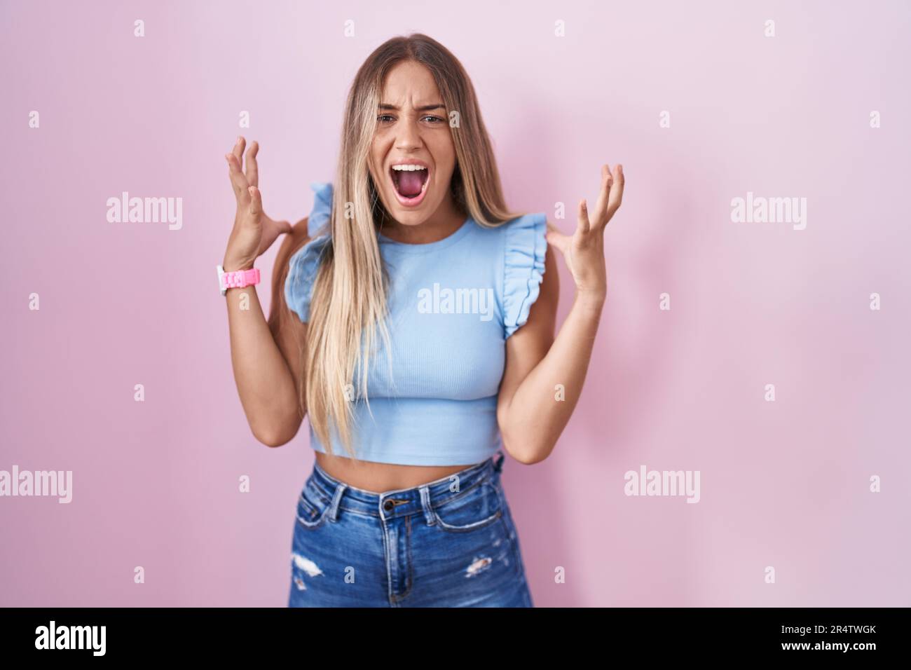 Young blonde woman standing over pink background crazy and mad shouting ...