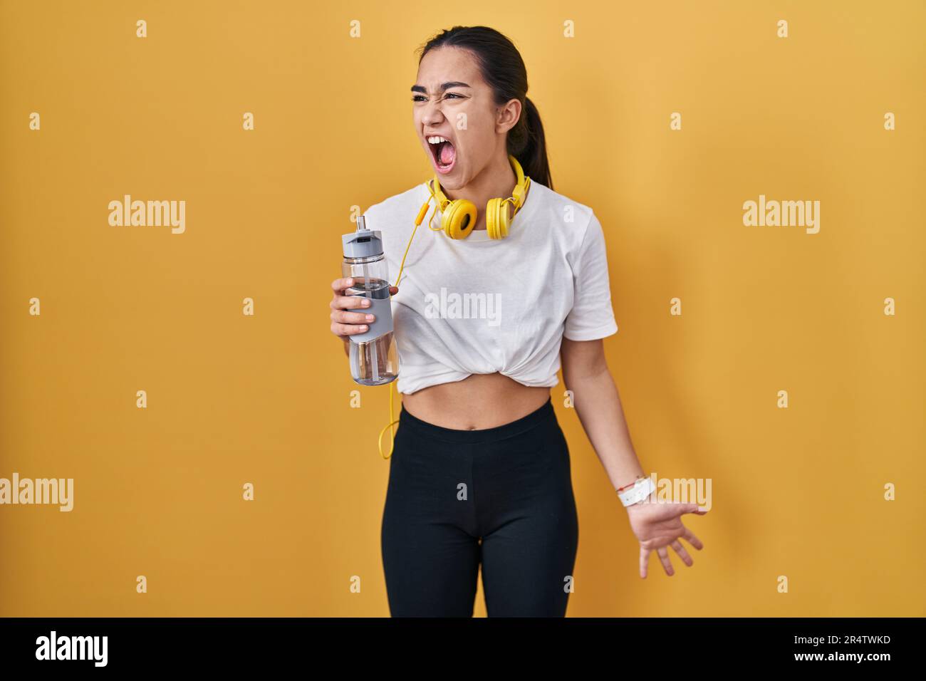Young south asian woman wearing sportswear drinking water angry and mad ...