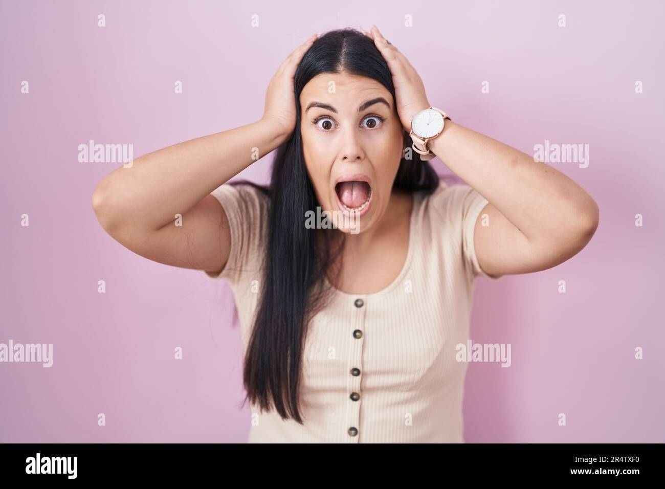 Young hispanic woman standing over pink background crazy and scared ...