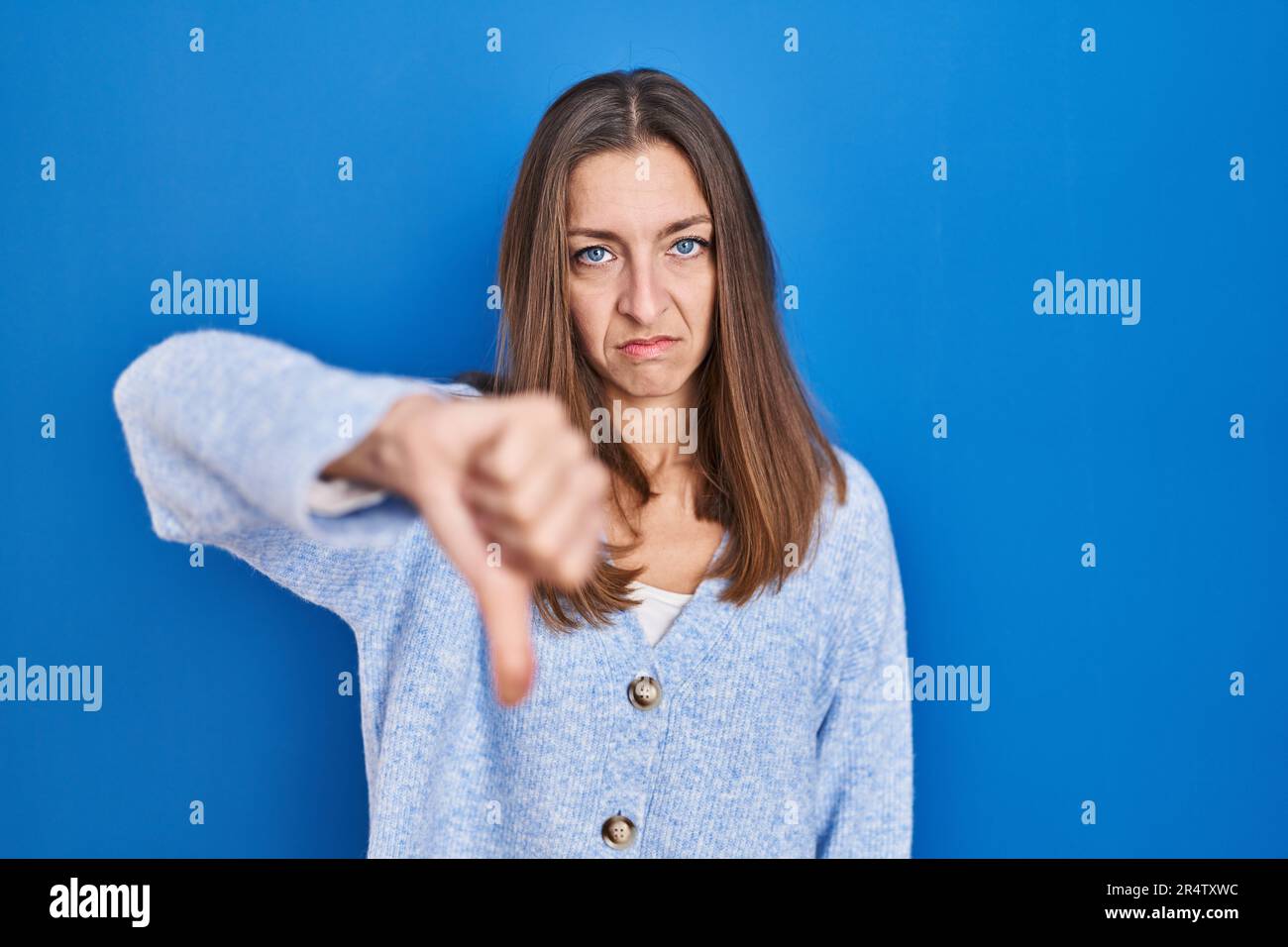 Young woman standing over blue background looking unhappy and angry ...