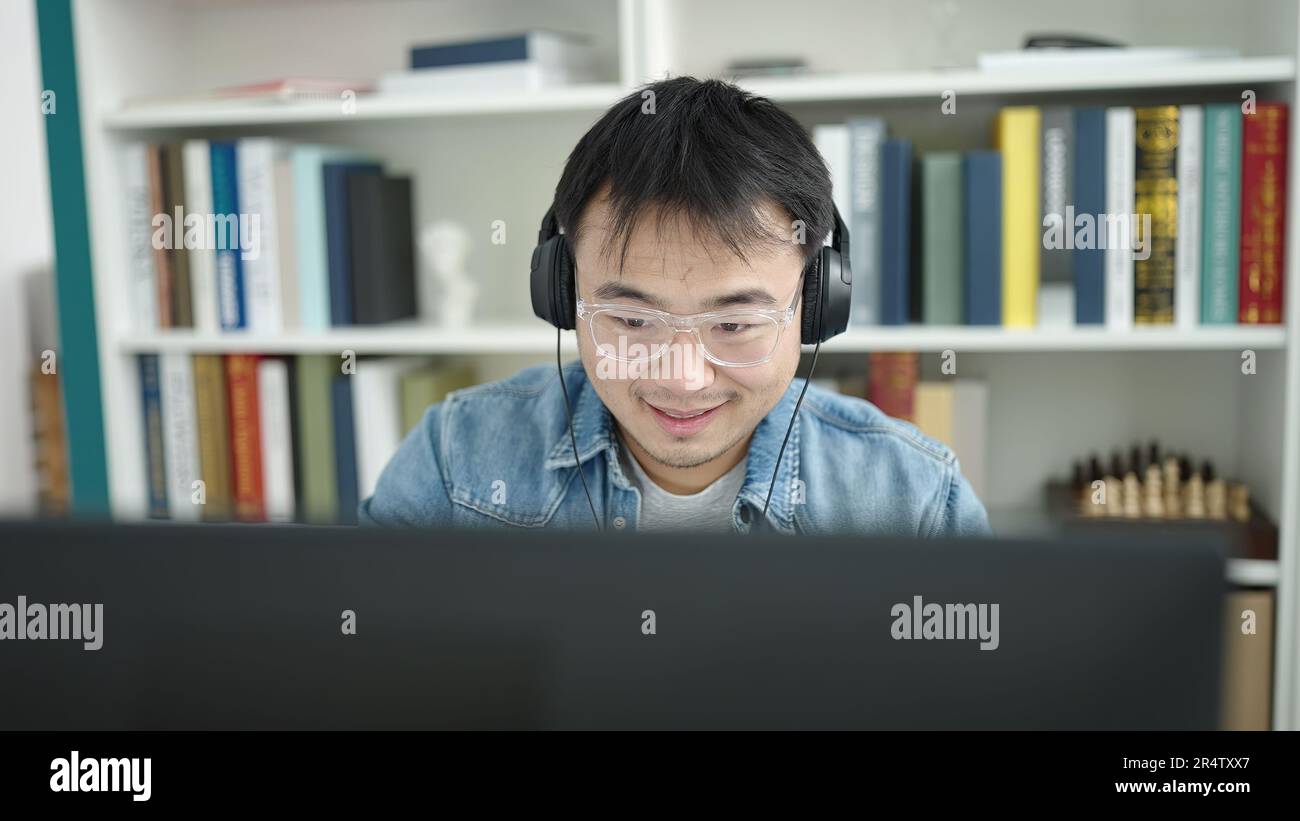 Young chinese man student using computer and headphones at library ...