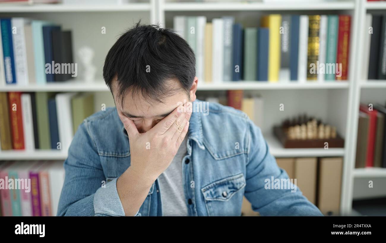 Young chinese man student sitting on table stressed at library ...