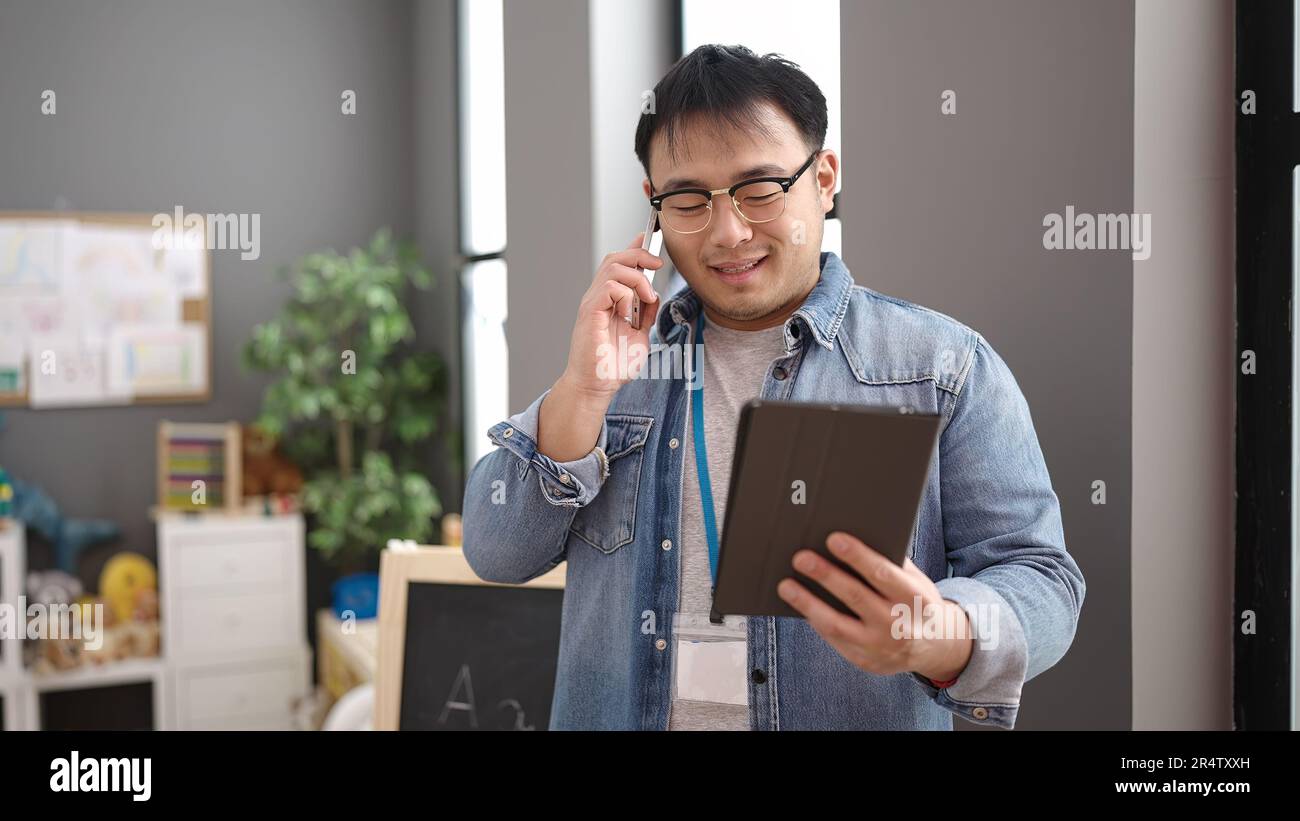 Young chinese man preschool teacher using touchpad talking on ...